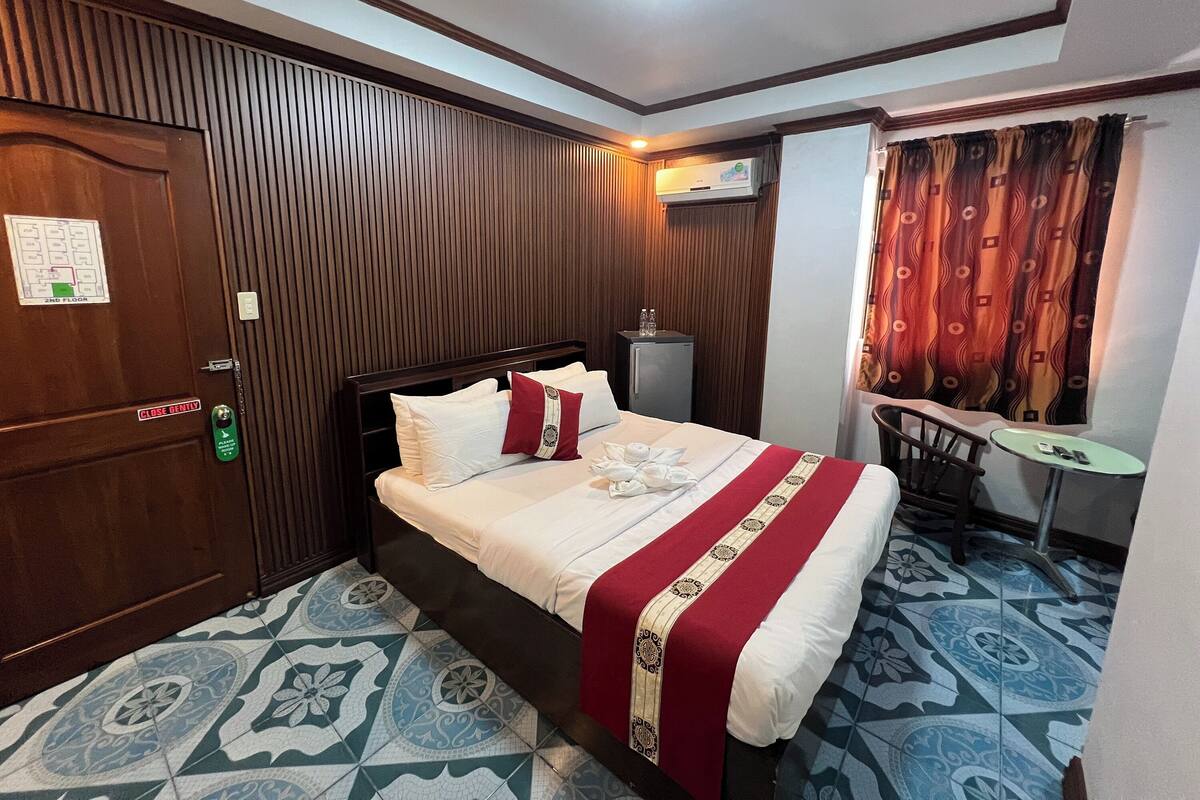 Quarto de hotel com cama, uma pequena mesa, uma cadeira, um guarda-roupa e uma porta com a placa '2º andar'.