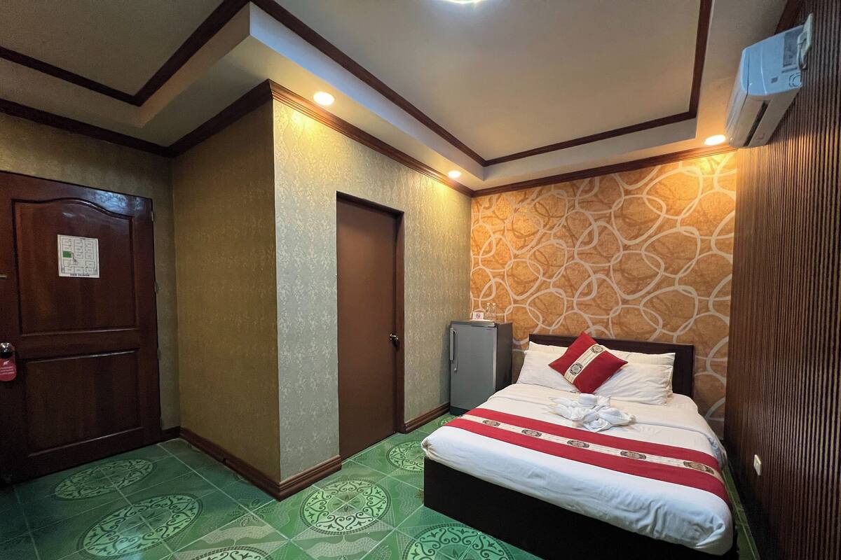 Quarto de hotel com uma cama, um guarda-roupa, um pequeno armário e pisos verdes estampados.