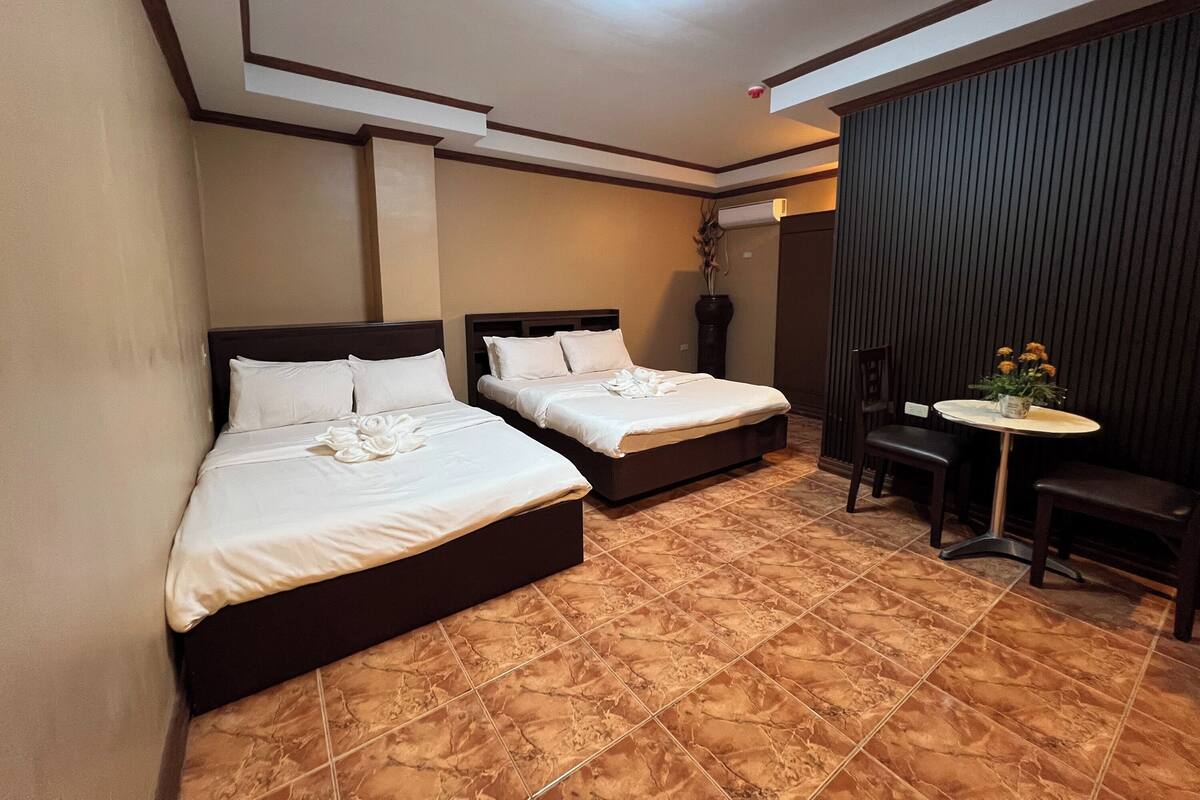 Quarto de hotel com duas camas, uma mesinha com um vaso de flores e uma cadeira.