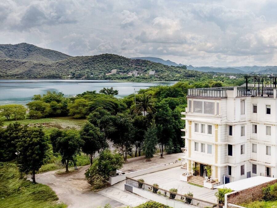 Um edifício de vários andares com telhado plano, cercado por vegetação exuberante e um corpo de água ao fundo.