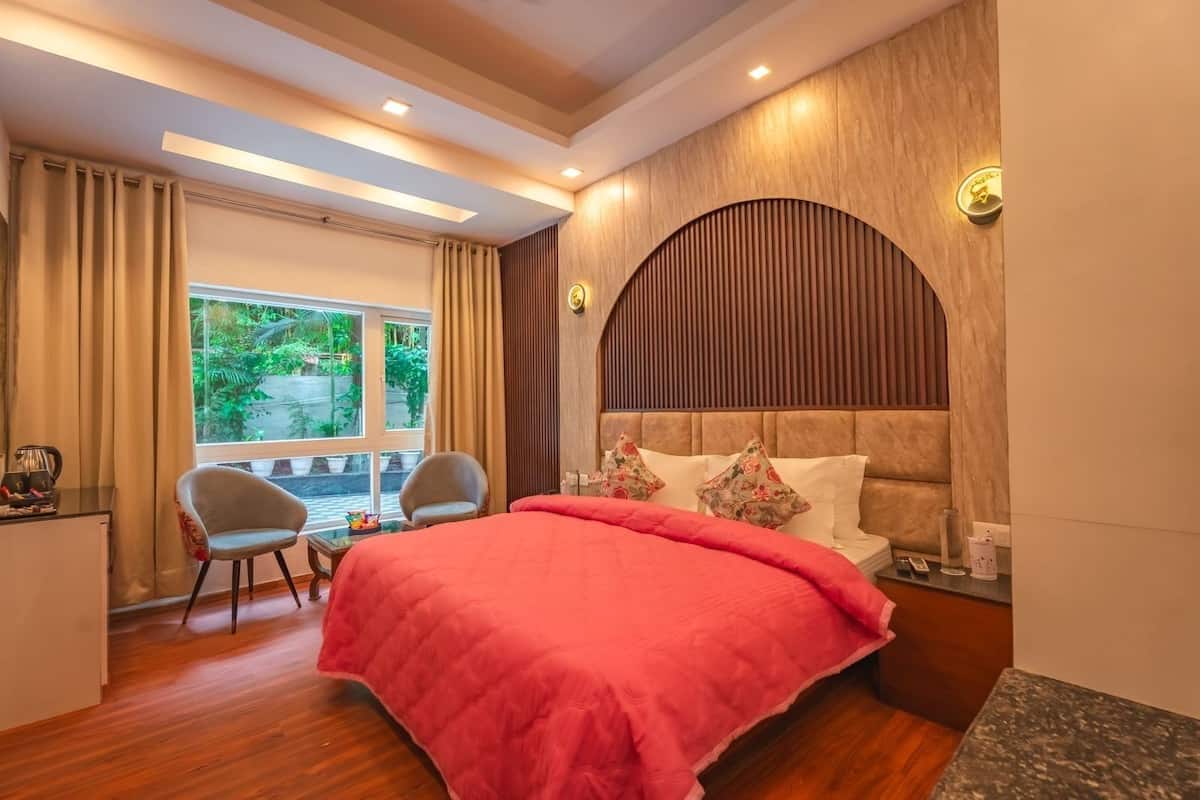 Quarto de hotel com uma cama grande, duas cadeiras, uma mesa de trabalho e vista para o verde lá fora.