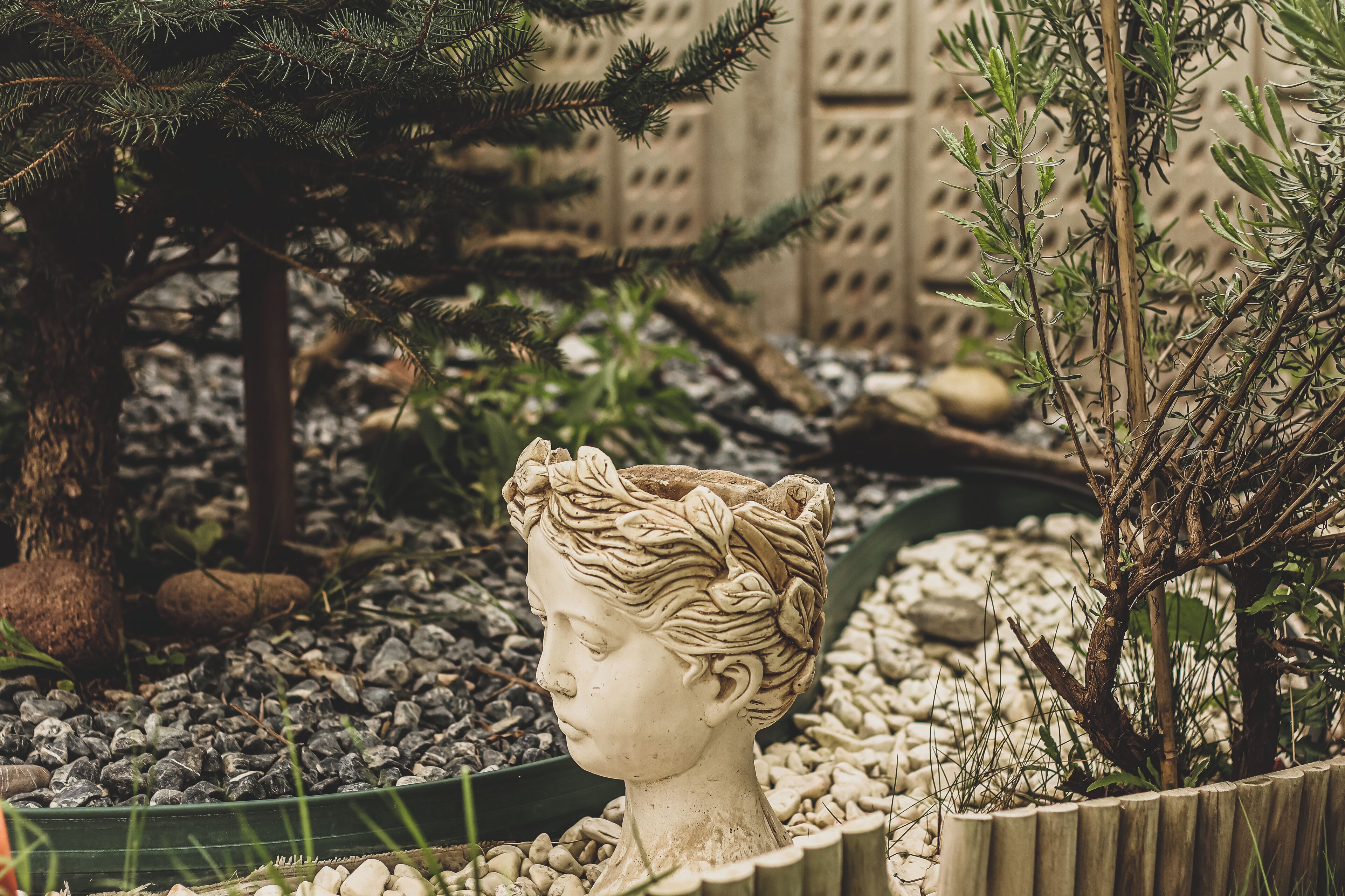 Um jardim com uma escultura de pedra, um pinheiro e uma cerca de madeira.
