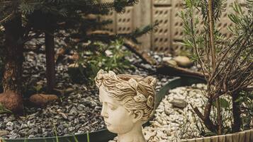 Um jardim com uma escultura de pedra, um pinheiro e uma cerca de madeira.