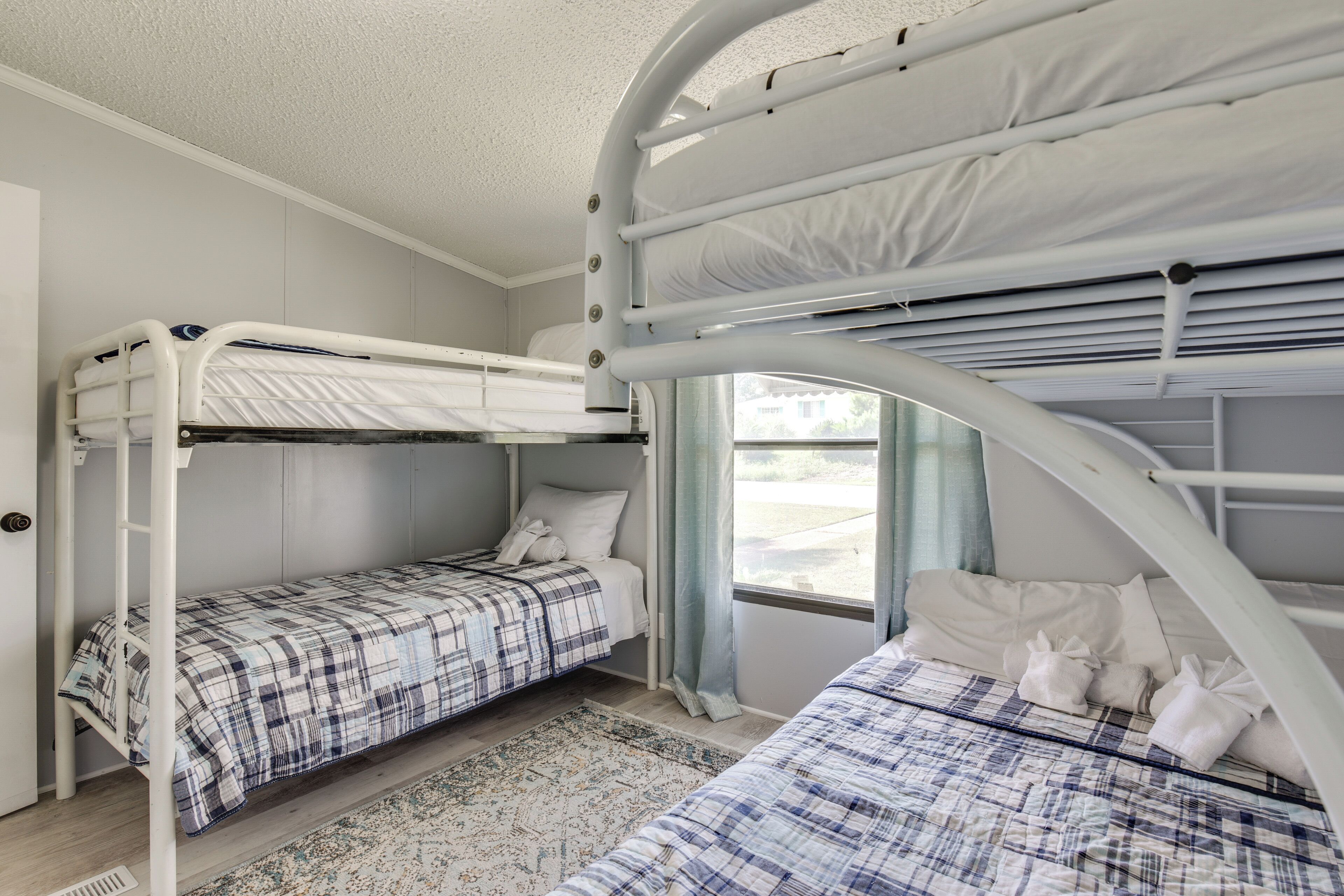 Quarto com beliche, coberta estampada, tapete e janela com cortinas.