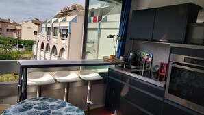 Uma varanda com área de bar, cozinha com forno embutido e vista para edifícios vizinhos.