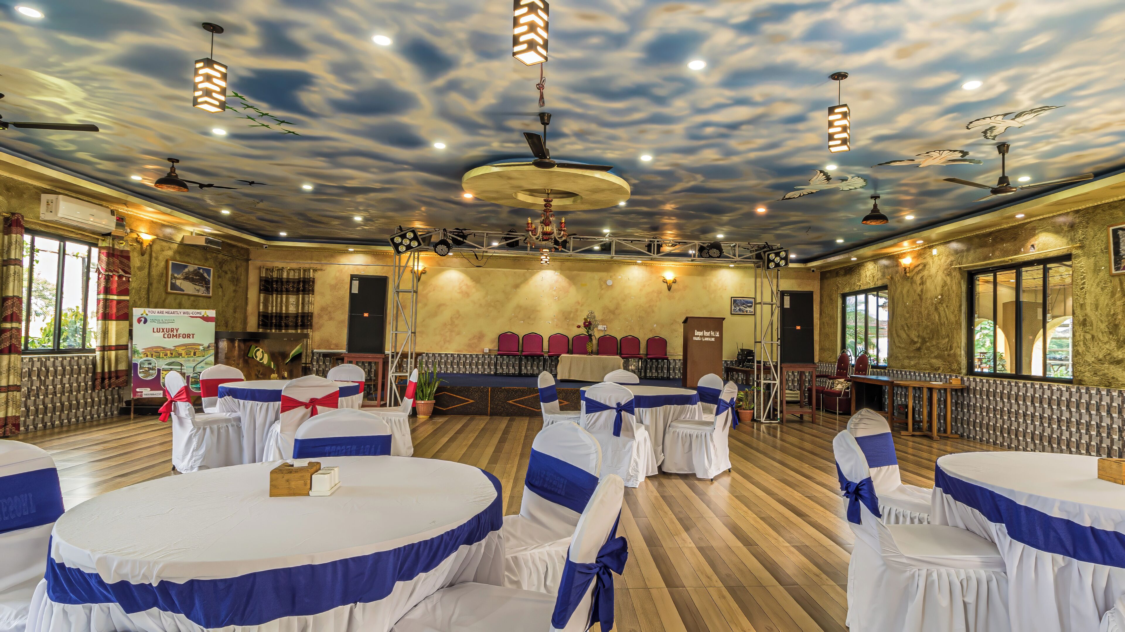 Uma sala de banquetes com mesas redondas, cadeiras vermelhas e um palco.
