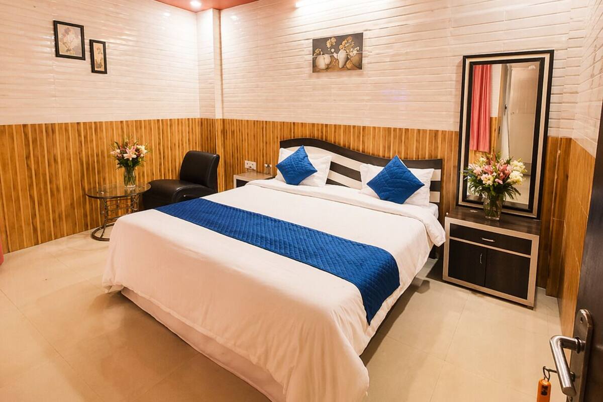 Quarto de hotel com cama, mesa de cabeceira, cadeira e espelho.