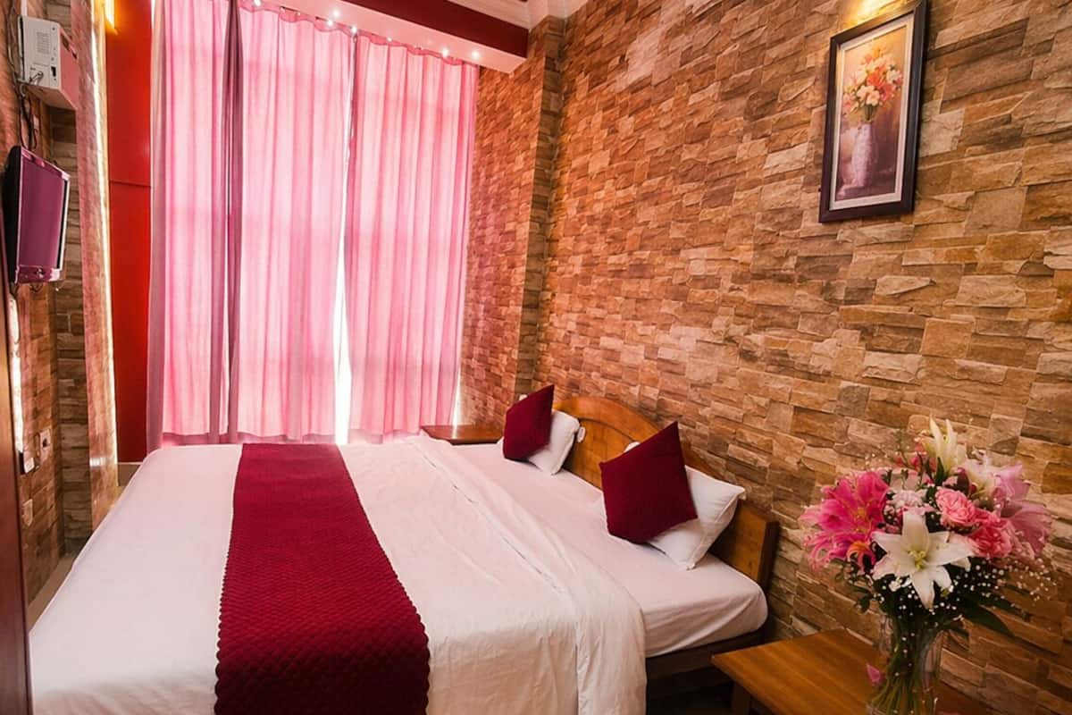 Quarto de hotel com uma cama grande, um banco de madeira, um vaso com flores e uma parede de pedra.