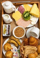 Uma bandeja com itens de café da manhã, incluindo presunto, queijo, ovos e doces.