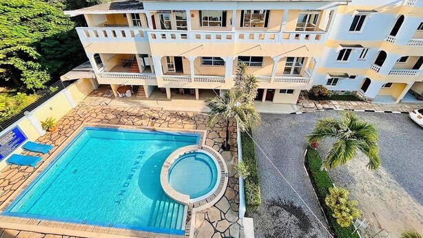 Um hotel de vários andares com piscina, área de estar externa e telhado com telhas vermelhas.