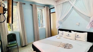 Quarto de hotel com cama grande, uma cadeira, ventilador de teto e cortinas.