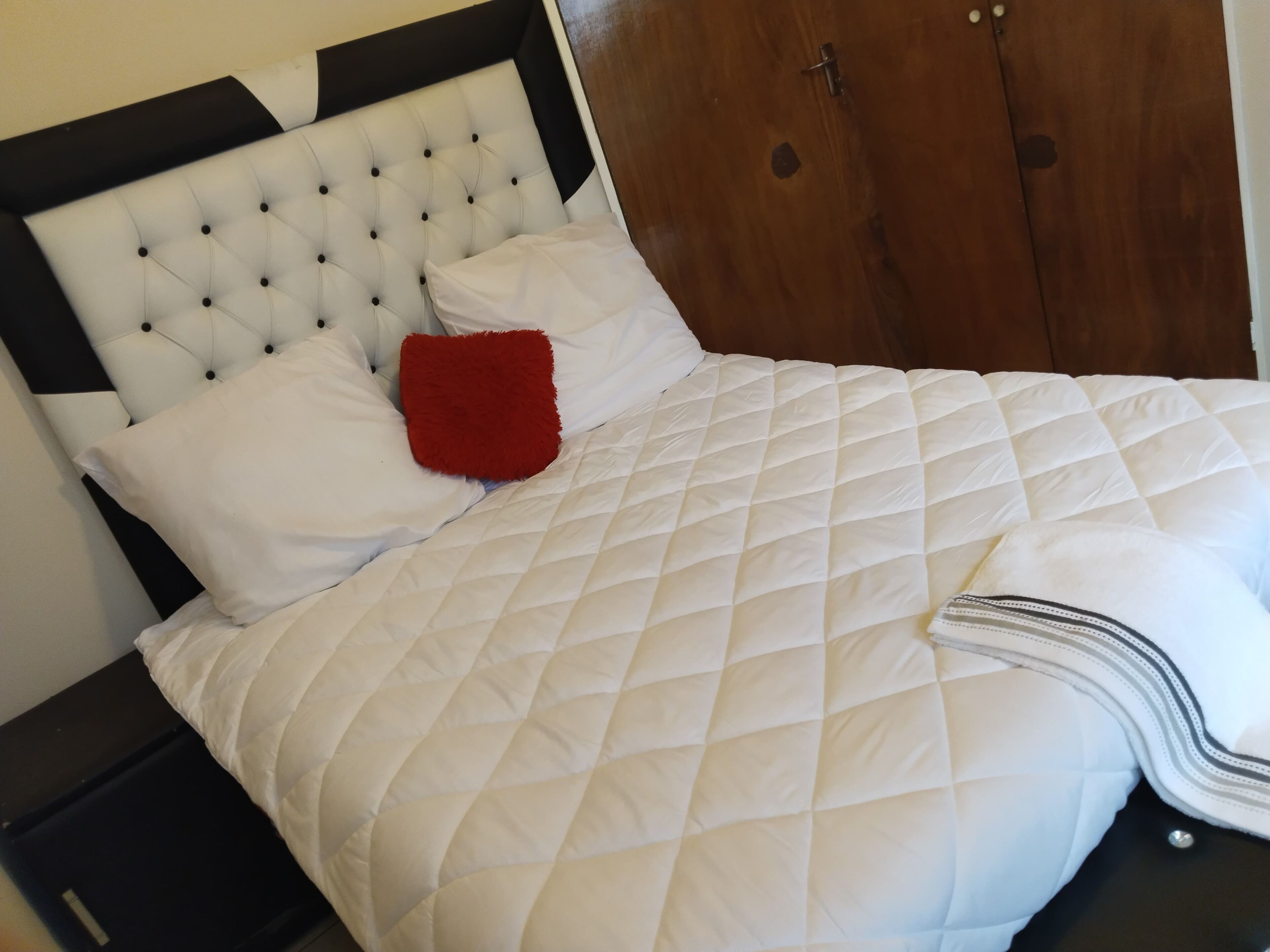 Uma cama com edredom branco acolchoado, um travesseiro vermelho e cabeceira preta.
