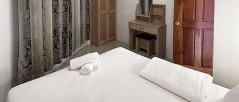 Quarto com cama grande, guarda-roupa de madeira, pequena escrivaninha com espelho e porta de madeira.