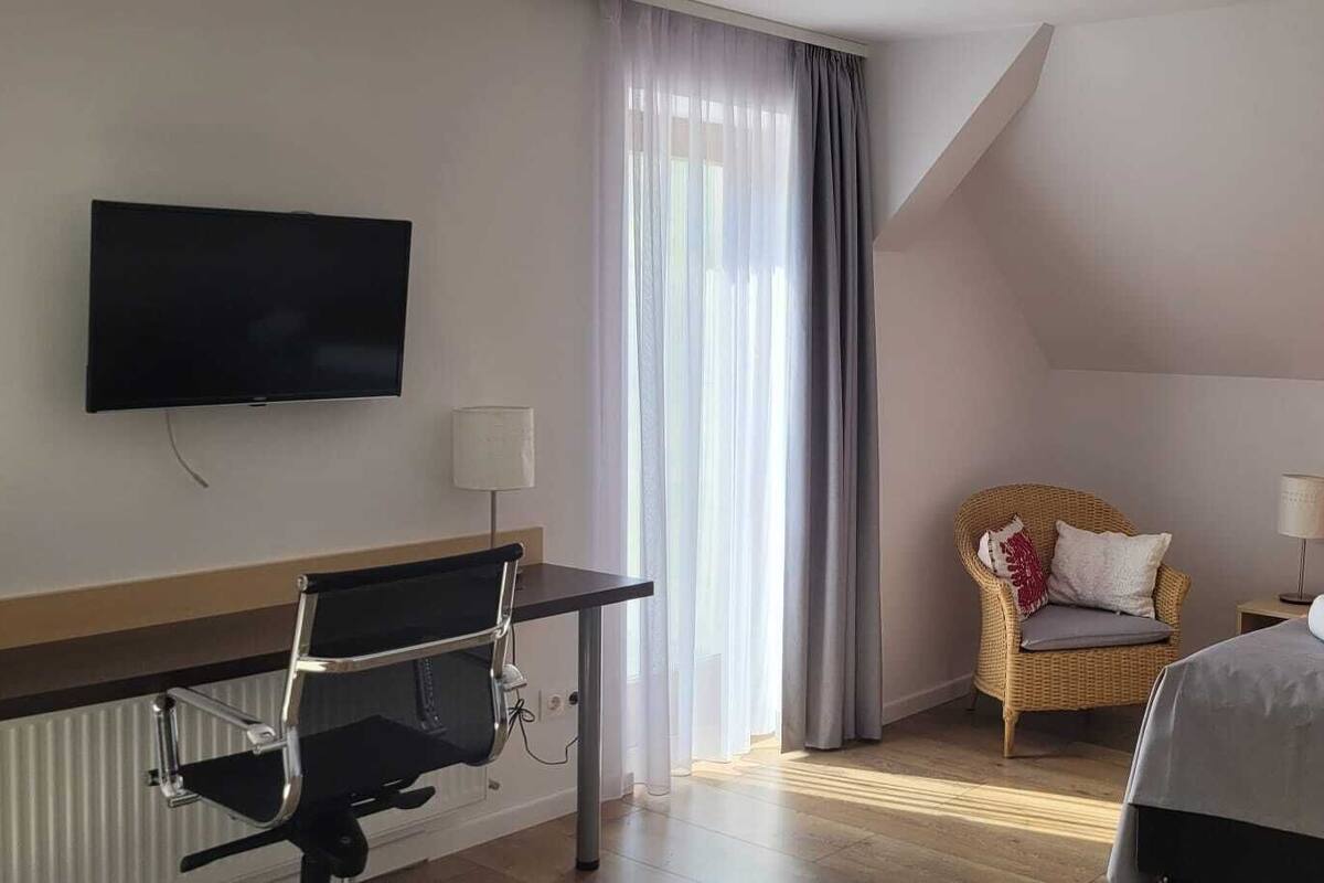 Quarto de hotel com cama, escrivaninha, cadeira, televisão e janela com cortinas.