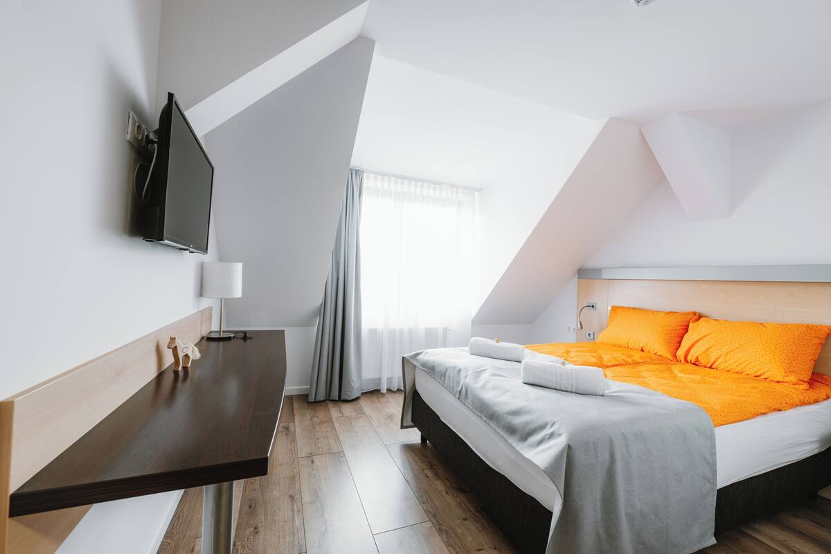 Quarto de hotel moderno com cama, mesa de cabeceira e televisão de tela plana fixada na parede.