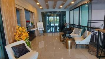 Um saguão de hotel com balcão de recepção, área de estar e grandes janelas.