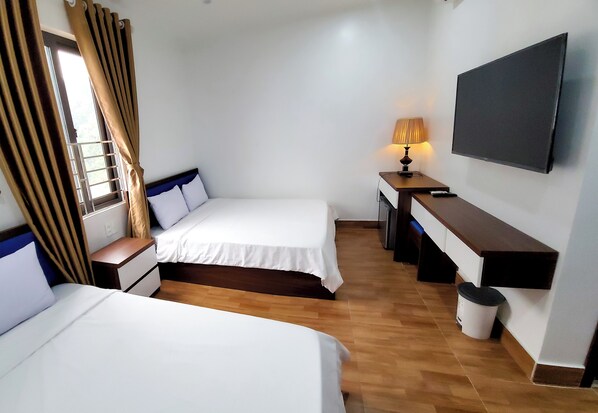 Quarto de hotel com duas camas, televisão, secretária com abajur e um cesto de lixo.