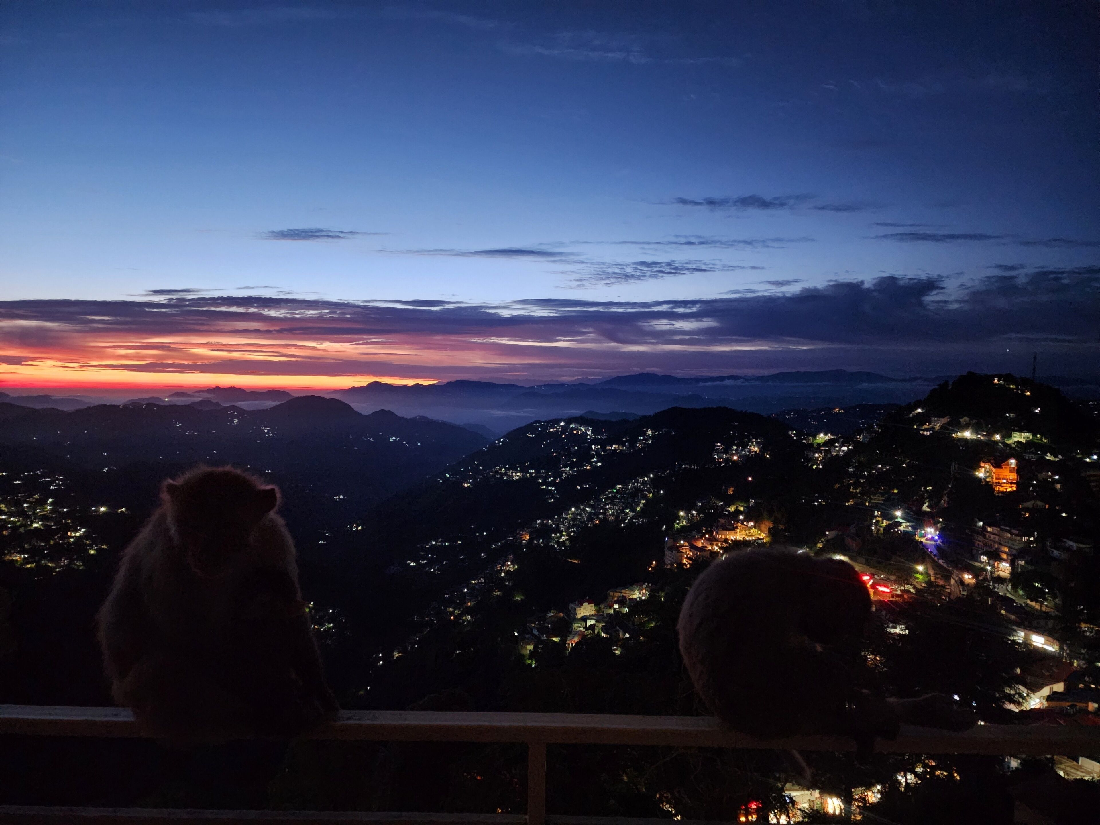 Vista noturna de uma região montanhosa com um horizonte urbano ao fundo.