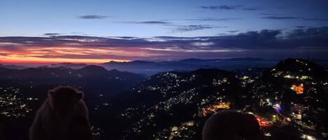 Vista noturna de uma região montanhosa com um horizonte urbano ao fundo.