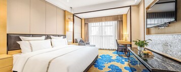 Quarto de hotel com uma cama grande, uma escrivaninha com cadeira, televisão e banheiro com espelho e pia.