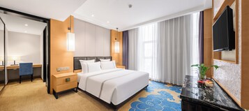Quarto de hotel com cama, mesa de cabeceira, escrivaninha, cadeira, televisão e banheiro com espelho.