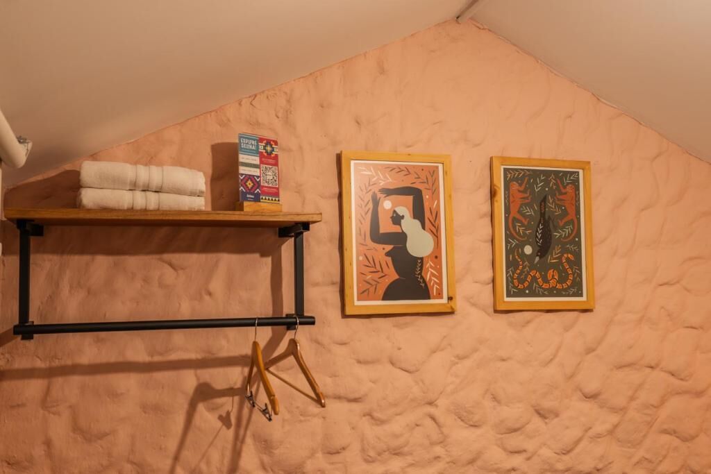 Quarto com teto inclinado, prateleira com toalhas dobradas e duas obras de arte emolduradas na parede.