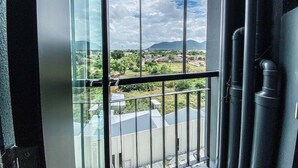 Vista de uma varanda com guarda-corpo de metal, com vista para uma paisagem com edifícios e montanhas sob um céu parcialmente nublado.