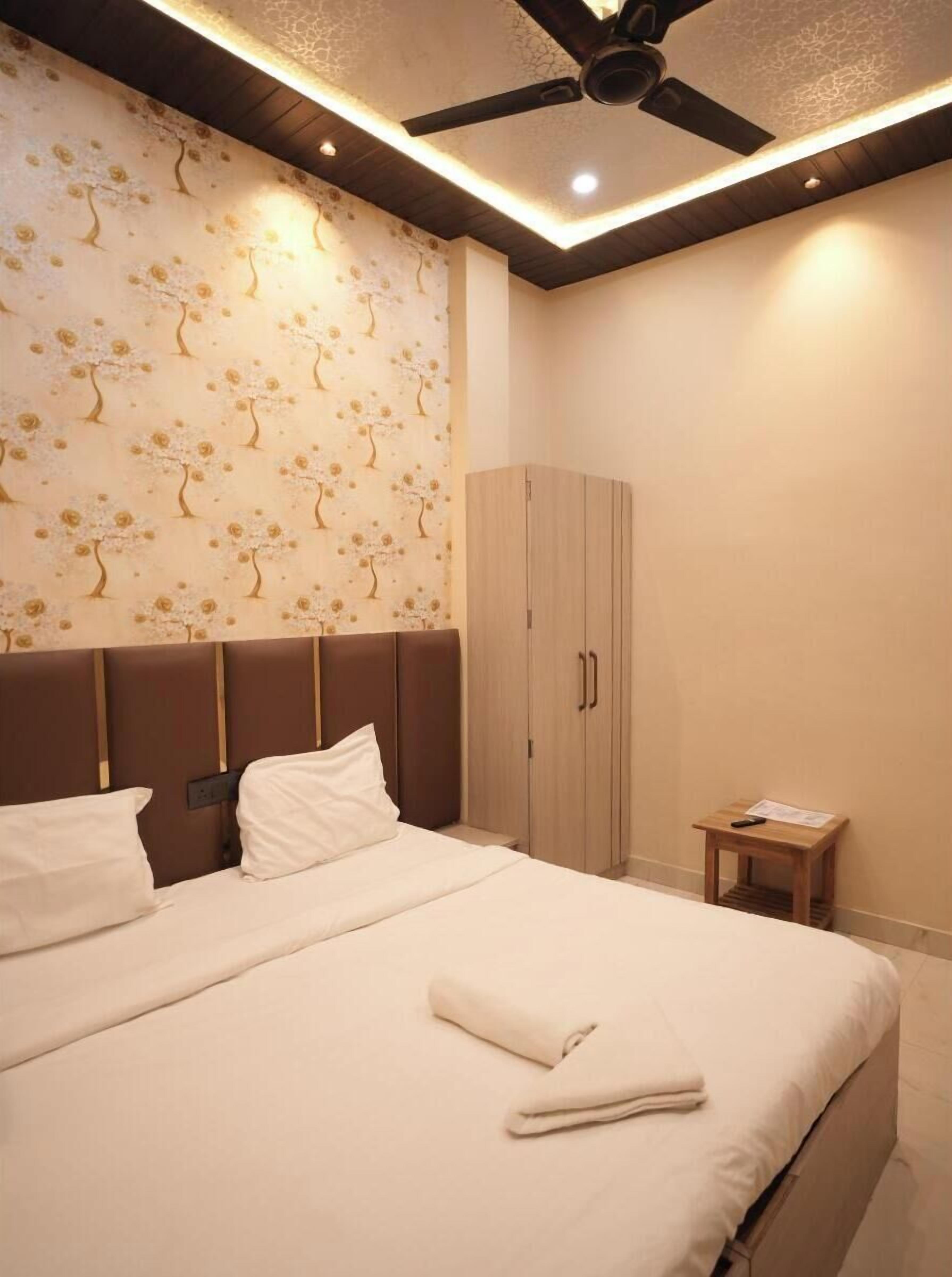 Quarto com cama, guarda-roupa, mesa pequena e ventoinha no teto.