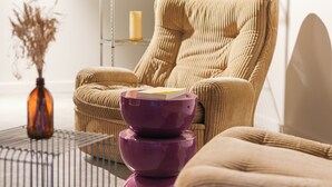 Uma poltrona bege estofada com uma tigela decorativa roxa sobre uma mesa.
