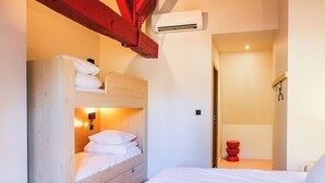 Quarto com uma cama beliche, uma cama de solteiro, uma cadeira vermelha e um aparelho de ar condicionado branco.