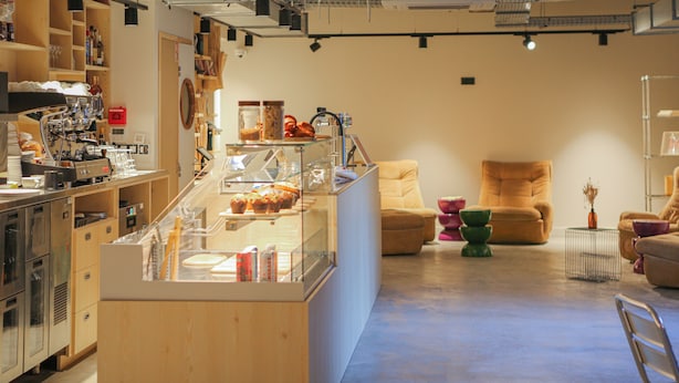 Um café moderno com balcão de madeira, área de estar e equipamentos de cozinha.