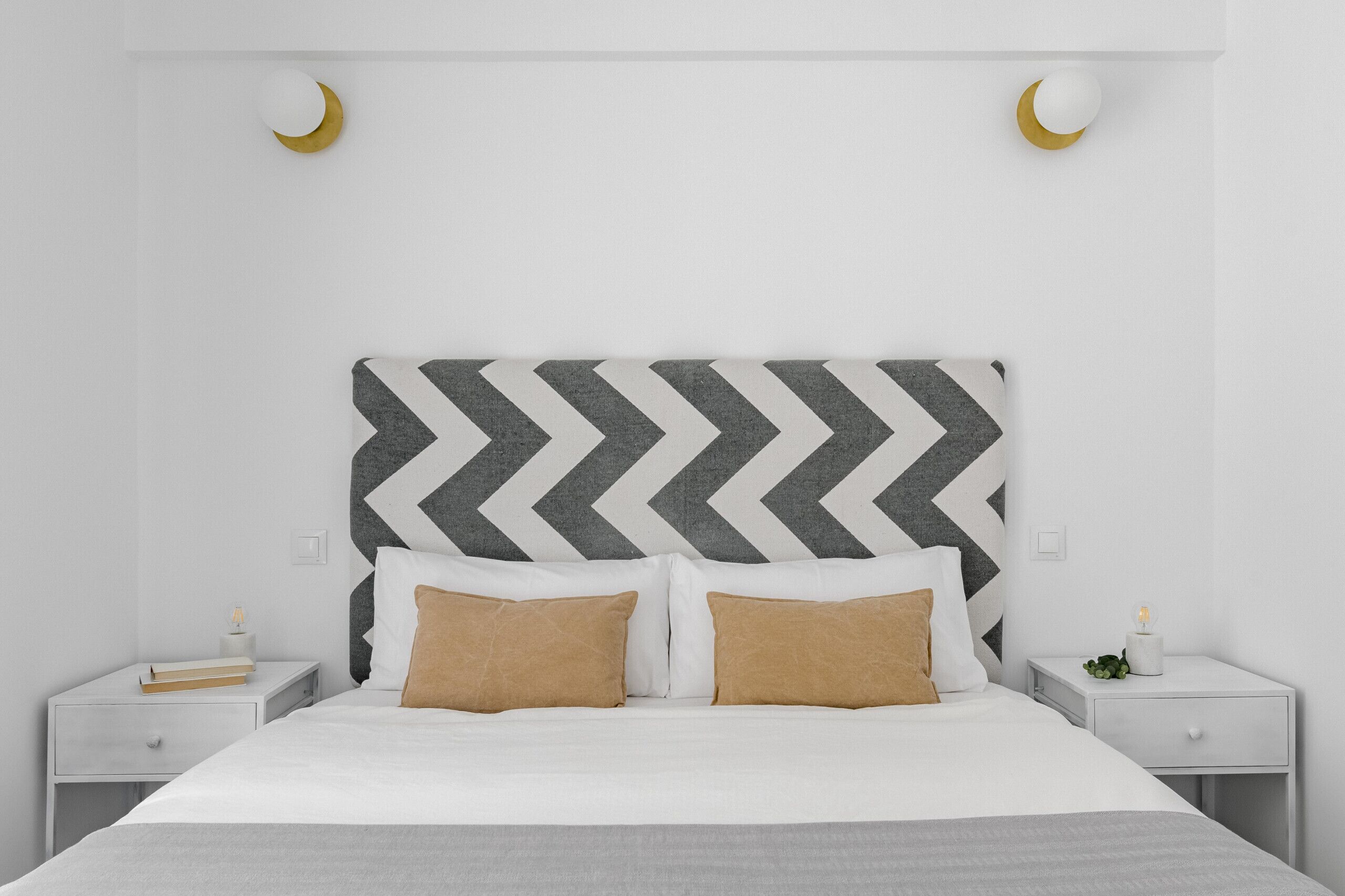 Quarto bem arrumado com uma cama grande, duas mesas de cabeceira e uma mesinha de cabeceira fixada na parede.