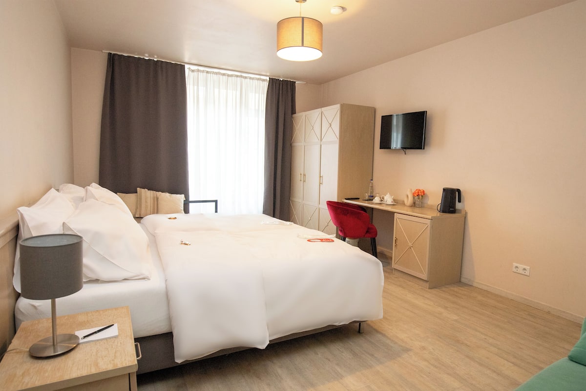 Quarto de hotel com uma cama, escrivaninha, cadeira, televisão e guarda-roupa.