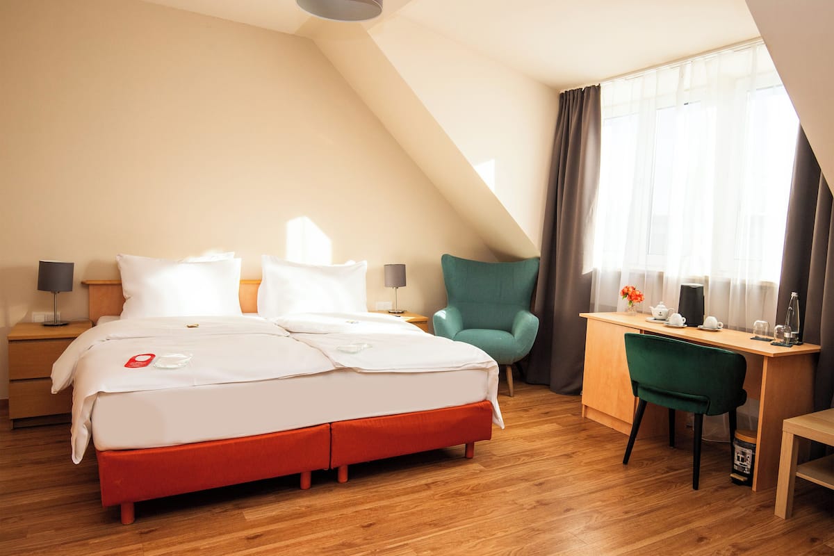 Quarto de hotel com cama, secretária, cadeira e janela com cortinas.