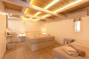 Quarto de hotel com cama, mesa de cabeceira, abajur e uma mesinha com um cesto.