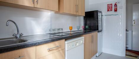 Cozinha moderna com armários de madeira, pia de aço inoxidável e bancada preta. Há potes de vidro e copos coloridos na bancada.