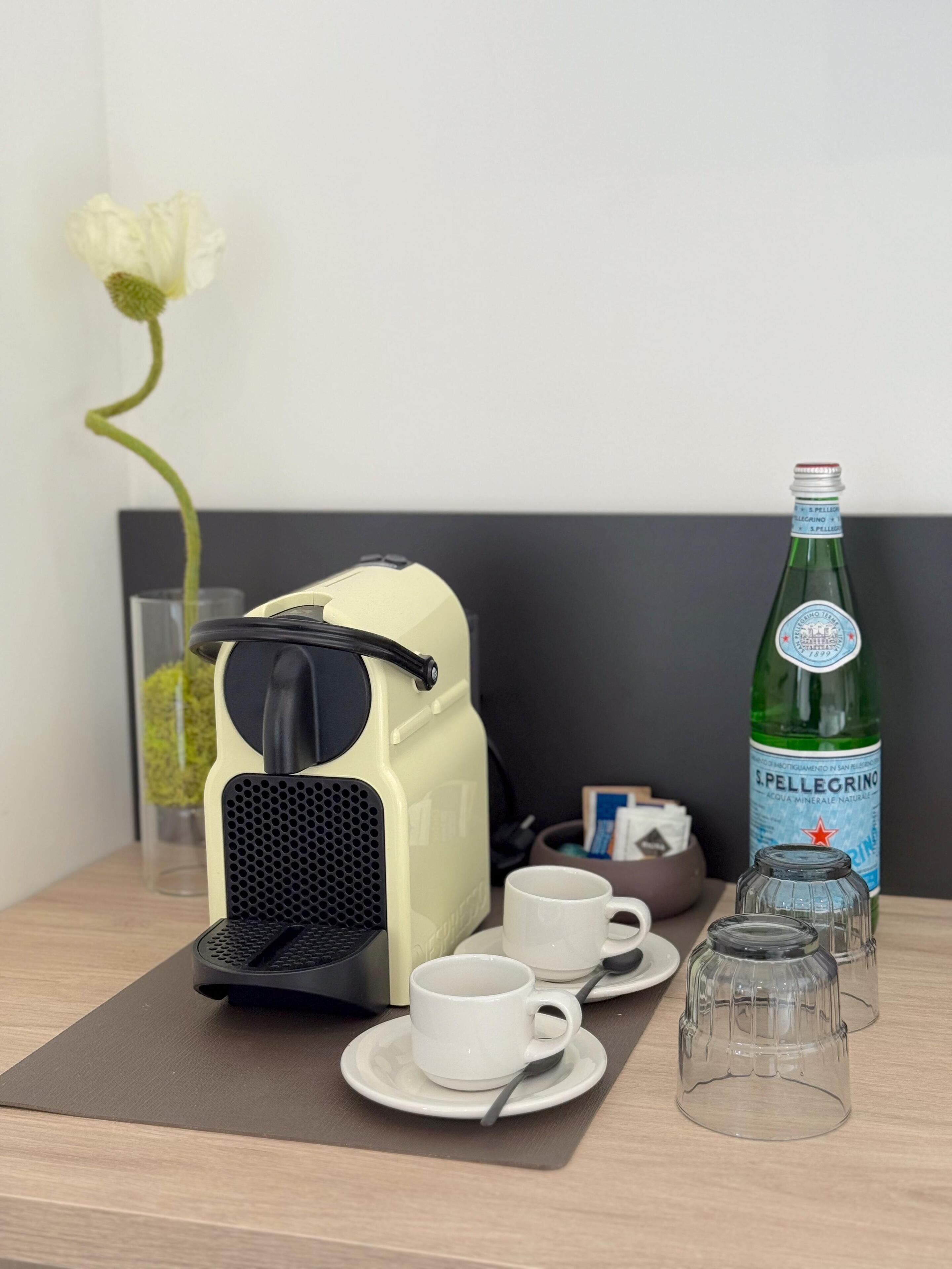 Uma cafeteira, duas chávenas, um copo e uma garrafa de água Pellegrino sobre uma mesa.
