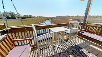 Um deck de madeira com mesa e cadeiras, com vista para um corpo d'água e campos.