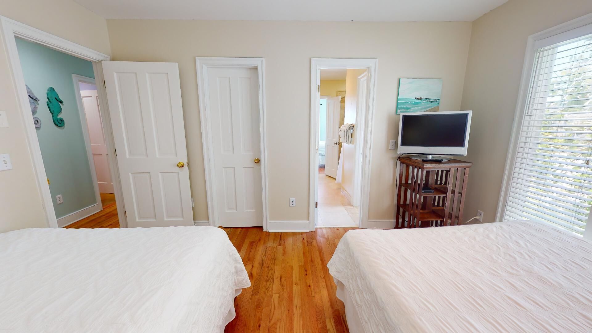Quarto com duas camas, uma televisão sobre suporte de madeira e uma porta que dá para outro cômodo.