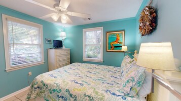 Quarto com cama, cômoda, televisão e uma pintura na parede.