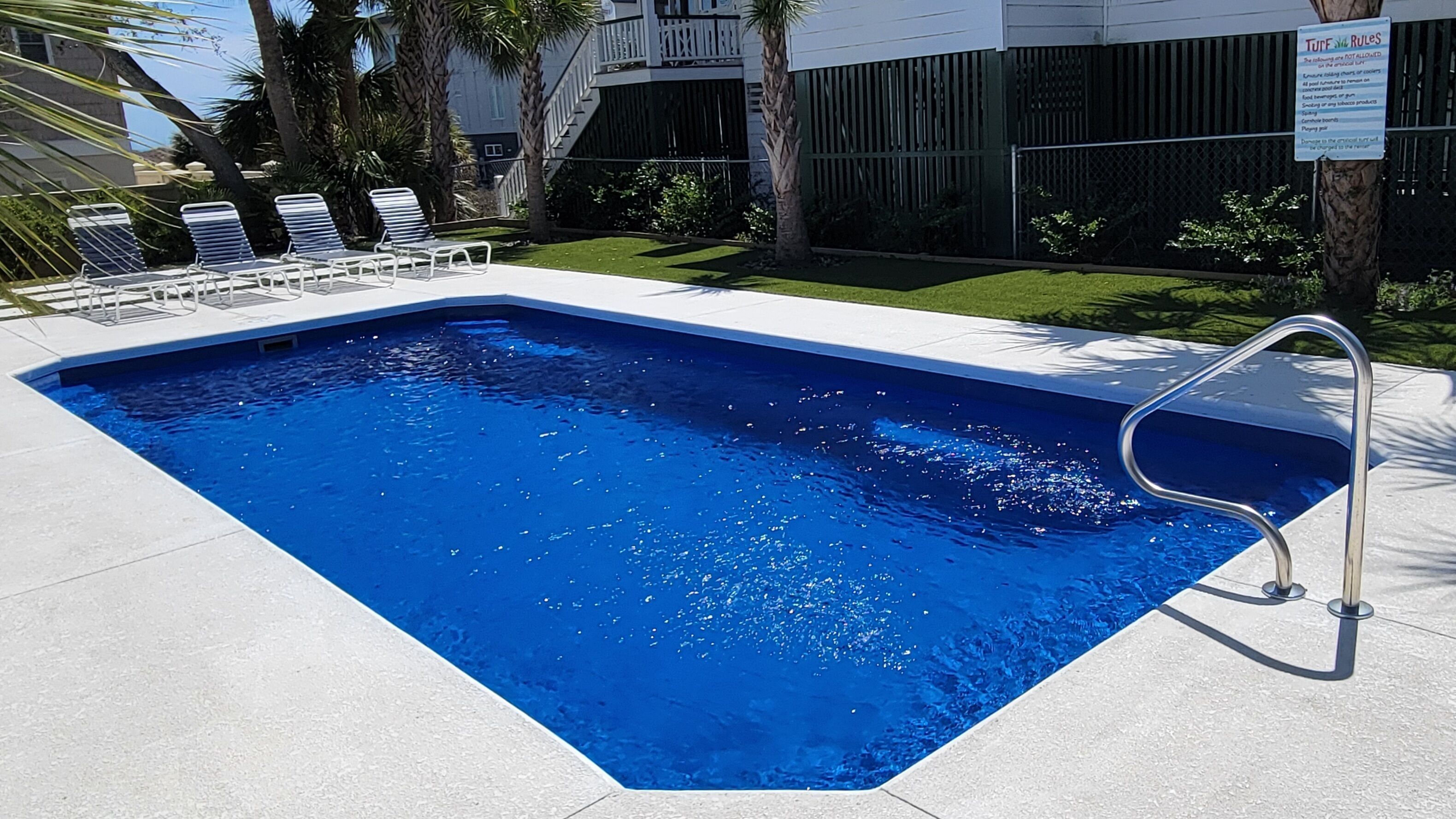 Piscina retangular com uma escada de metal de um lado, rodeada por um deck de concreto.