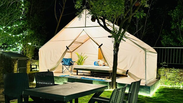 Uma tenda montada em uma área gramada, com uma mesa e cadeiras à frente.