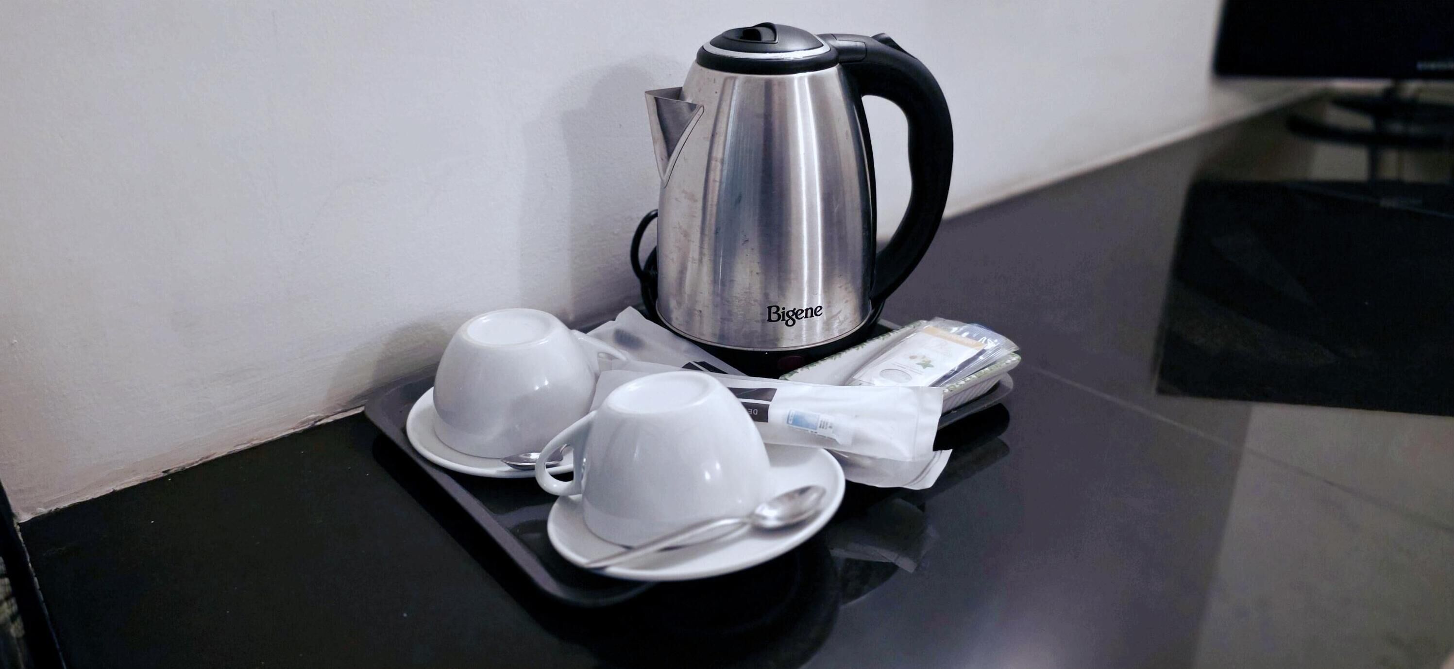 Uma bandeja com uma chaleira de prata, duas xícaras brancas, uma colher e um pacote de lenços de papel sobre uma mesa preta.