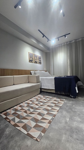 Um quarto moderno com um sofá, uma cama com cobertura azul, um tapete estampado e luminárias no teto.