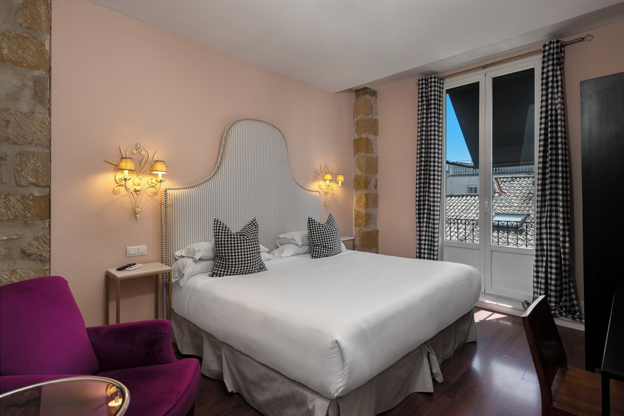 Quarto de hotel com cama, cadeira, mesa de cabeceira e janela com cortinas.