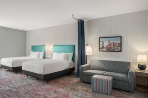 Quarto de hotel com duas camas, um sofá, um tapete estampado e um quadro na parede.