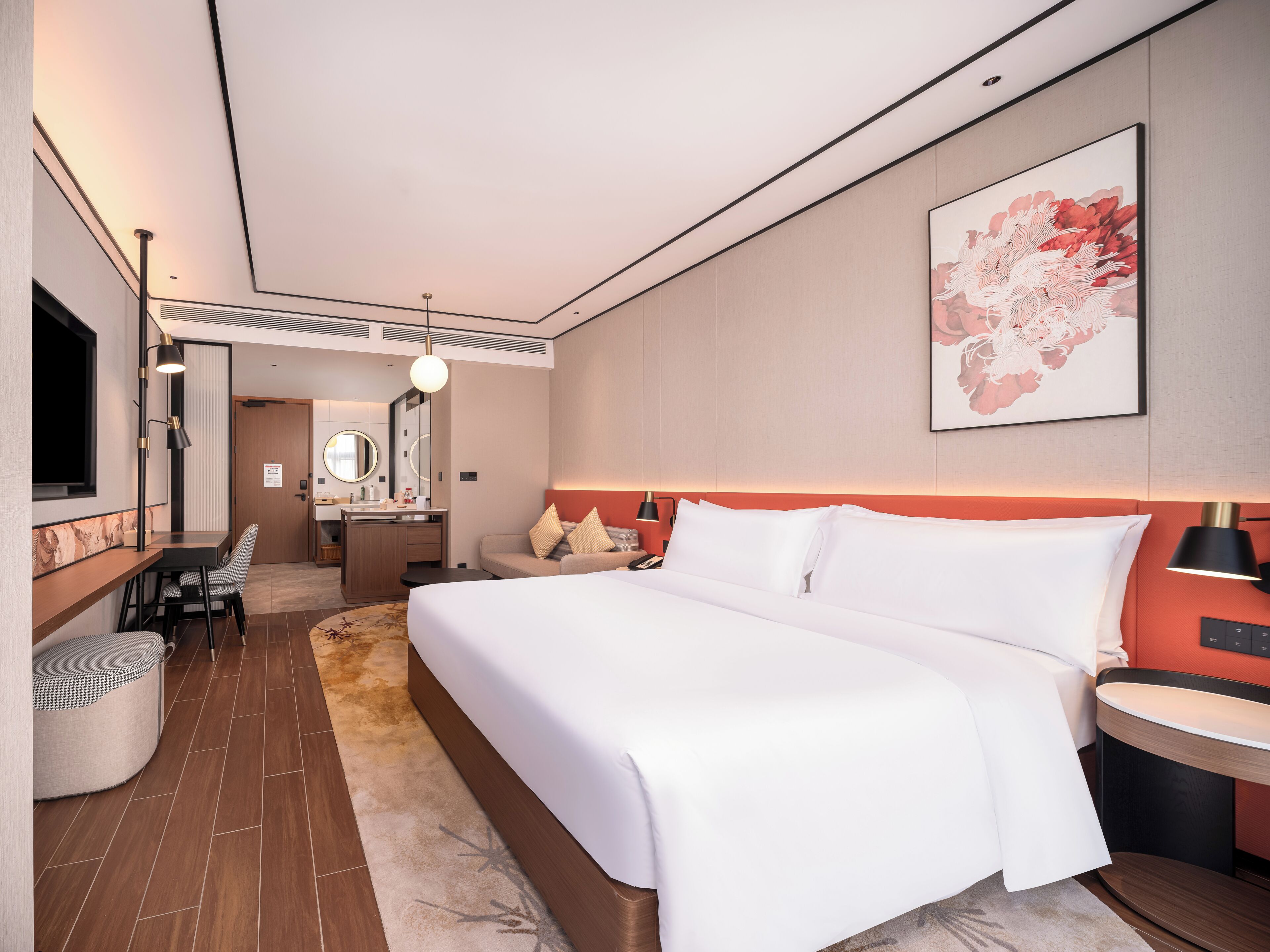 Quarto de hotel moderno com uma cama grande, uma escrivaninha, uma cadeira, toucador com espelho e televisão.