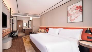 Quarto de hotel moderno com uma cama grande, uma escrivaninha, uma cadeira, toucador com espelho e televisão.