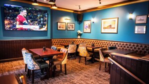Um restaurante com uma grande tela de televisão, cabines acolchoadas e quadros decorativos nas paredes.