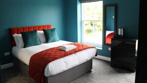 Quarto com cama, penteadeira e janela com vista para vegetação.